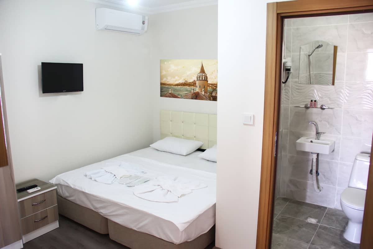 Quarto de hotel com cama, televisão, quadro e banheiro com pia e vaso sanitário.