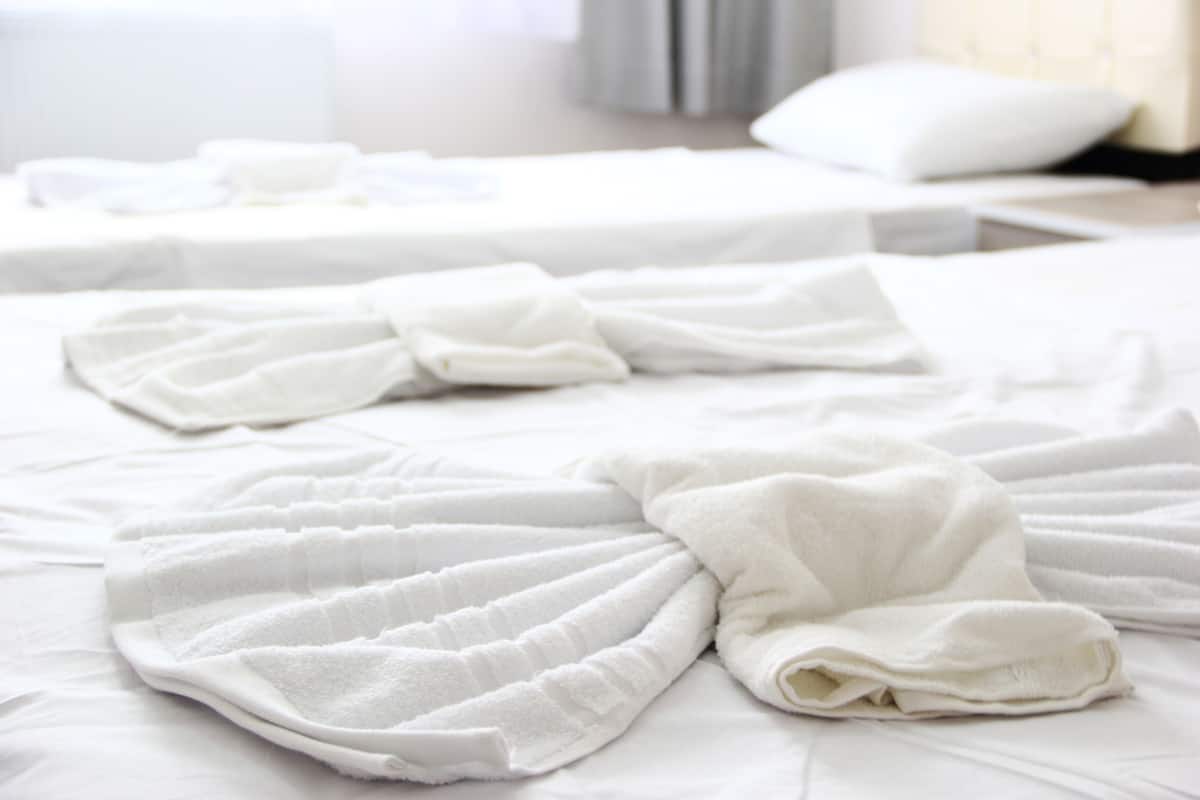 Cama bem arrumada com lençóis brancos e uma toalha branca dobrada.