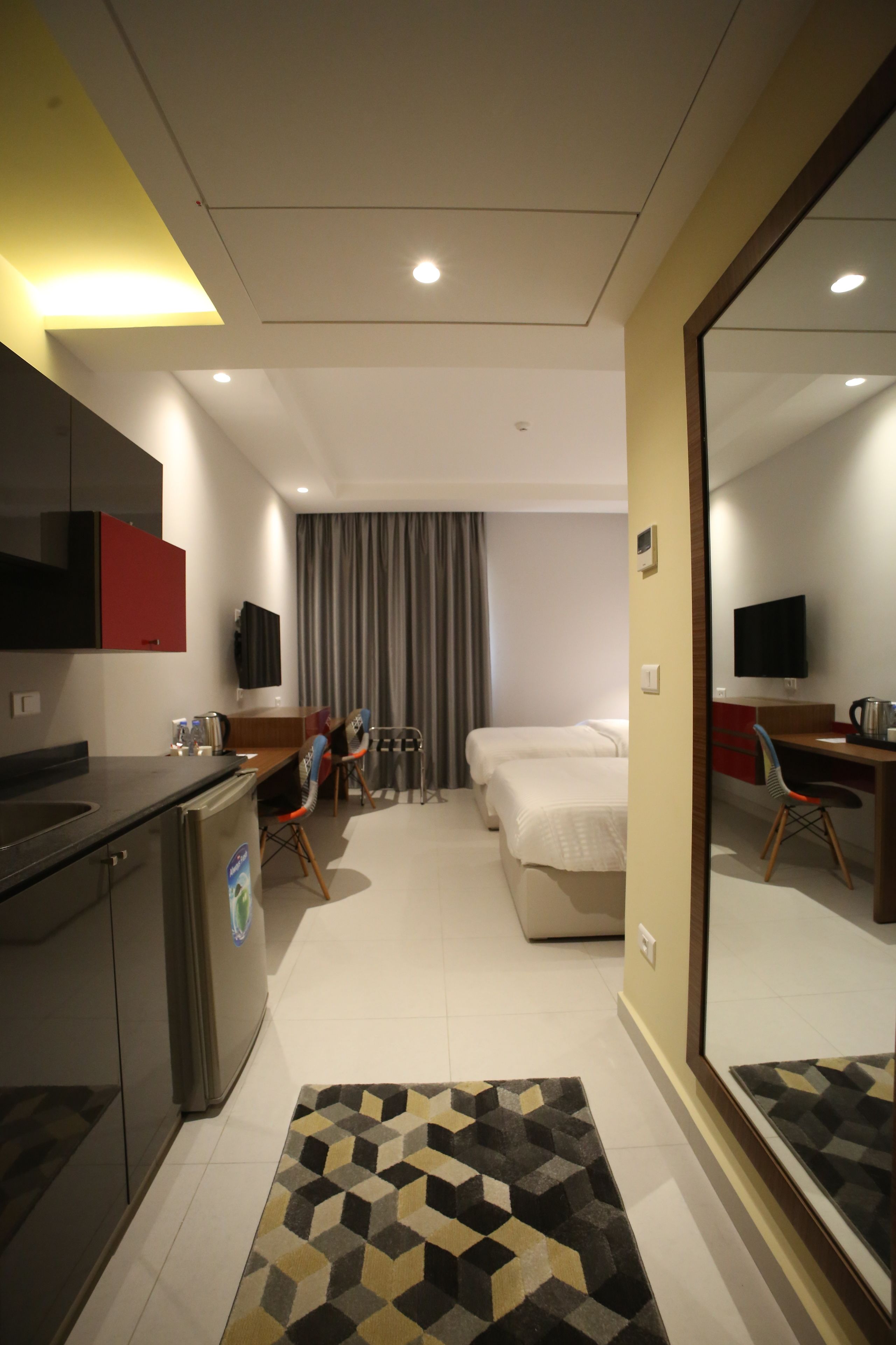 Quarto de hotel com cozinha compacta, duas camas, televisão e um espelho grande.