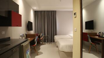Quarto de hotel com cozinha compacta, duas camas, televisão e um espelho grande.