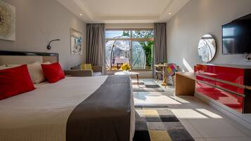 Quarto de hotel moderno com uma cama grande, uma escrivaninha, uma televisão e vista para o exterior.