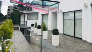 Um edifício moderno com área externa coberta, plantas em vasos e porta de vidro.
