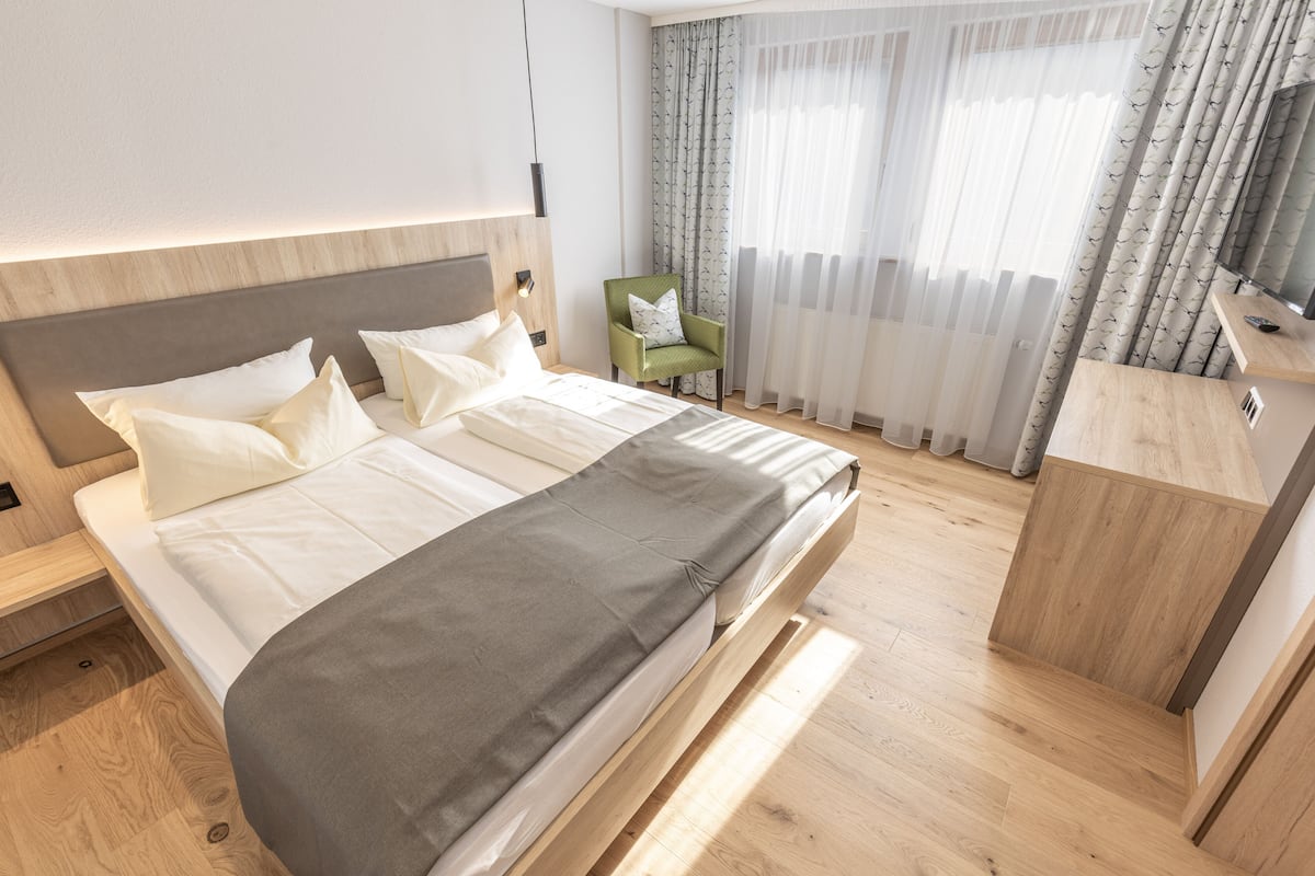 Quarto de hotel moderno com uma cama grande, uma cadeira, uma mesa e uma televisão.