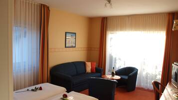 Quarto de hotel com sofá, uma mesa pequena com uma garrafa, televisão e cama com uma rosa.