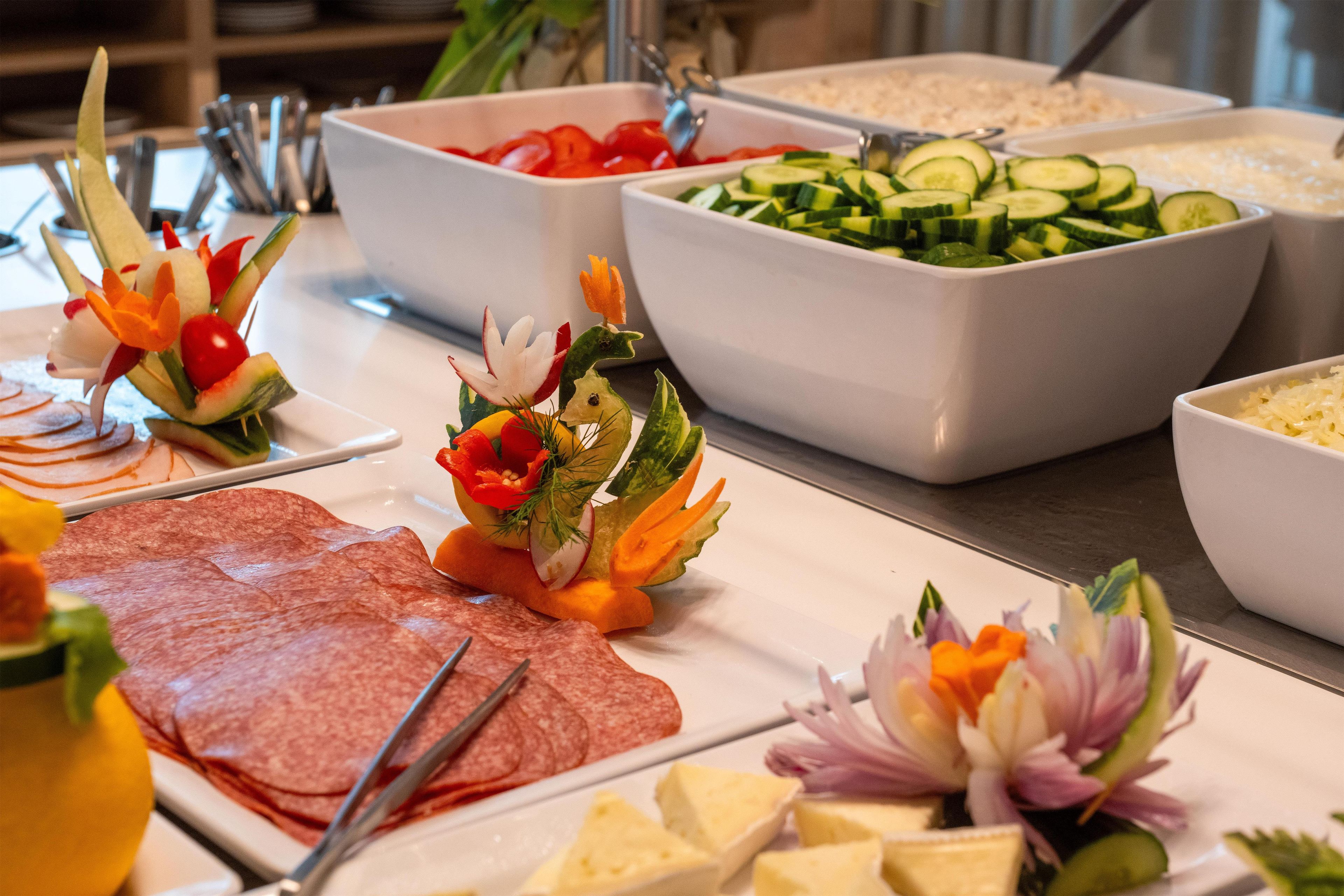 Buffet com diversos alimentos, incluindo carnes fatiadas, vegetais e um centro de mesa decorativo.