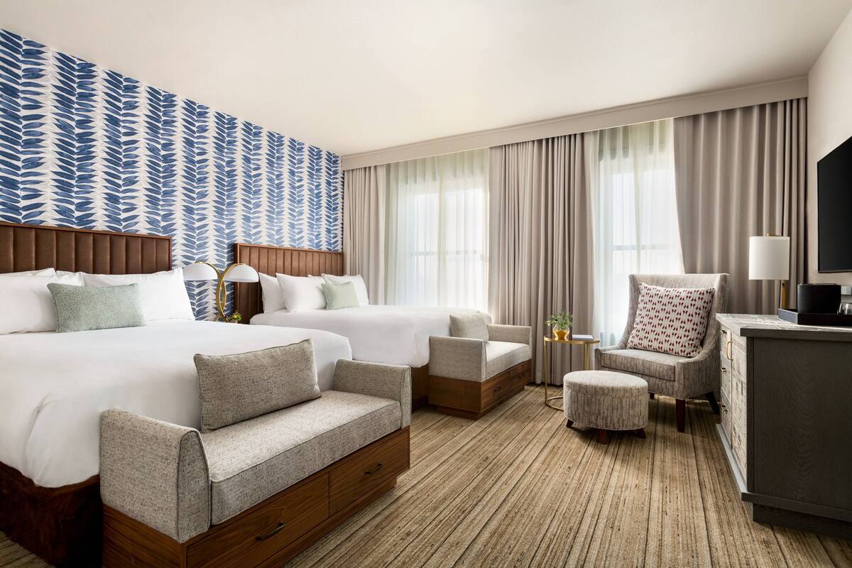 Quarto de hotel com uma cama grande, dois sofás, uma poltrona, uma escrivaninha e uma televisão.