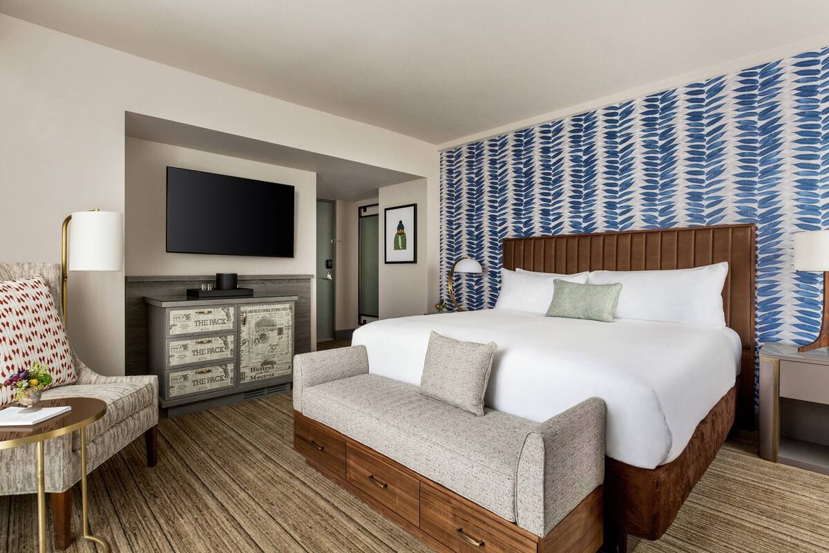 Quarto de hotel com uma cama grande, um sofá, uma TV, uma cômoda e parede com padrão.