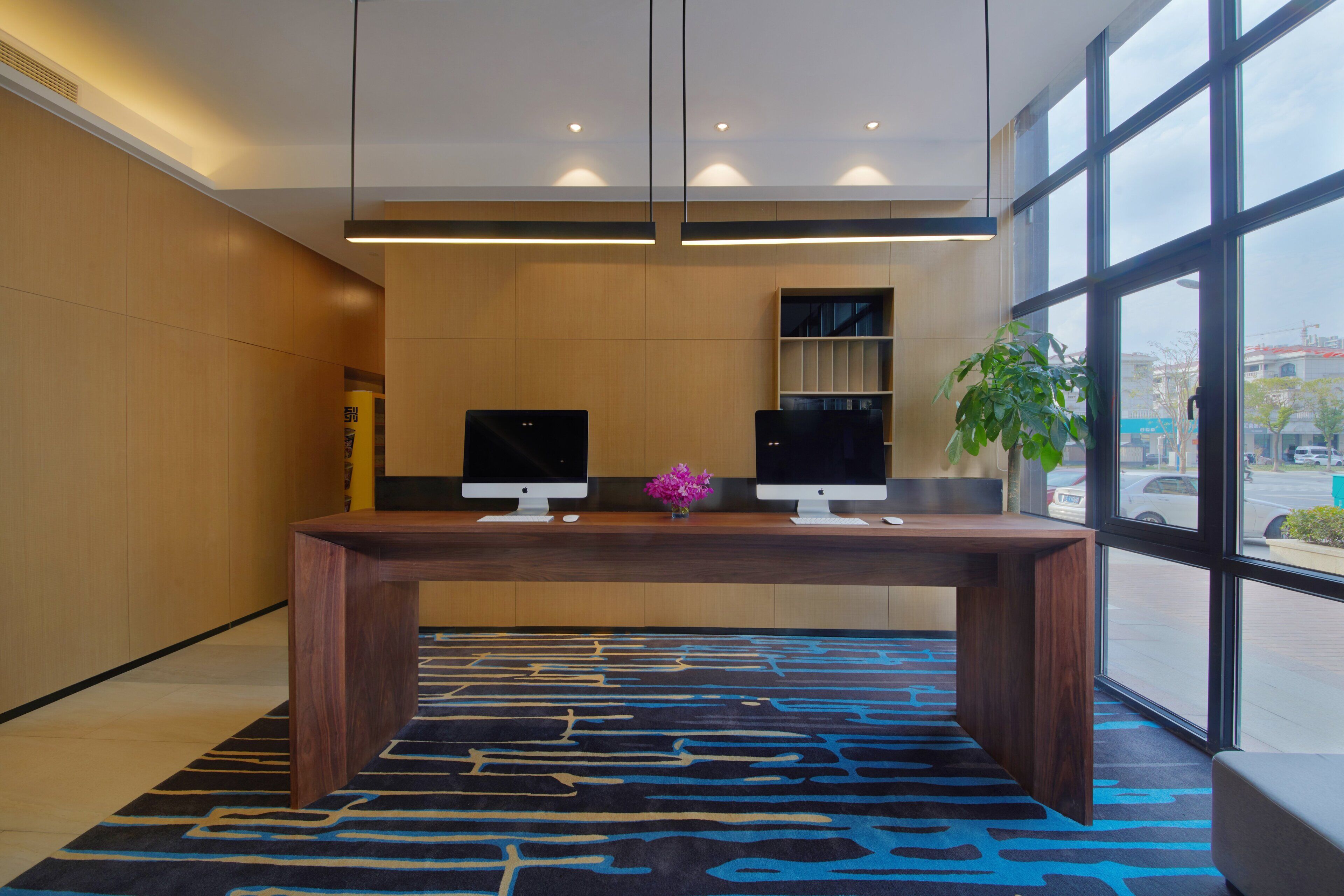Bancada de recepção com dois monitores, uma planta e um tapete com padrão azul e preto.