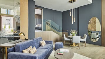 Uma sala de estar moderna com um sofá azul, uma área de jantar com uma mesa redonda e uma escada que leva a um andar superior.