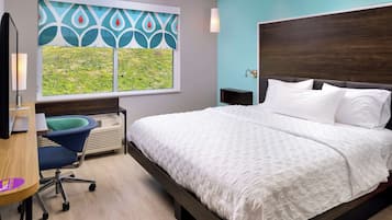 Quarto de hotel moderno com uma cama grande, uma escrivaninha com cadeira, uma janela com vista para o verde e uma parede de destaque em tom de verde-água.