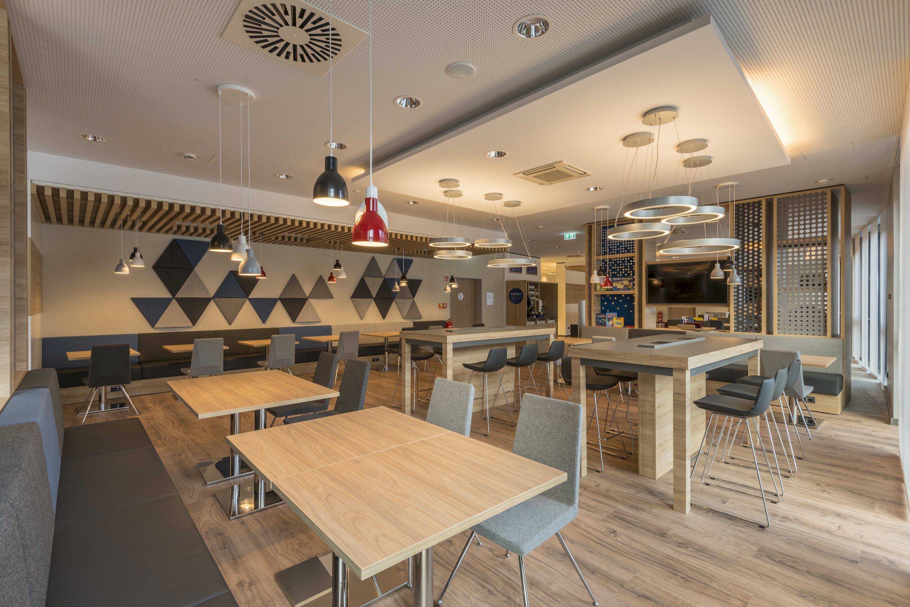 Interior moderno de restaurante com mesas e cadeiras altas, iluminação pendente e design geométrico na parede.