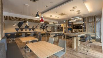 Interior moderno de restaurante com mesas e cadeiras altas, iluminação pendente e design geométrico na parede.