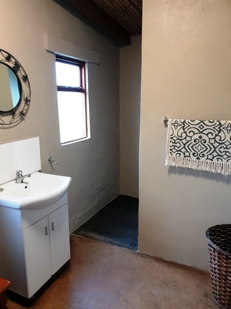 Uma casa de banho com uma pia branca, um espelho com moldura decorativa, uma janela e uma toalha estampada pendurada na parede.