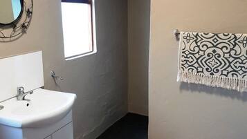 Uma casa de banho com uma pia branca, um espelho com moldura decorativa, uma janela e uma toalha estampada pendurada na parede.