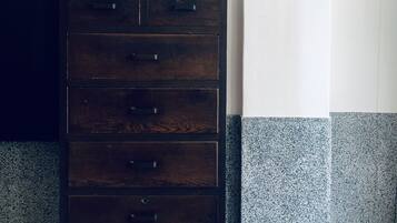 Uma cómoda de madeira escura com várias gavetas, um quadro emoldurado e uma orquídea num vaso, tudo em frente a uma parede com design de azulejos salpicados.
