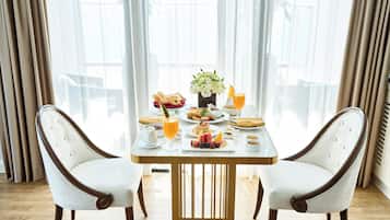 Mesa de jantar com itens de café da manhã, duas cadeiras estofadas e vista através de grandes janelas.