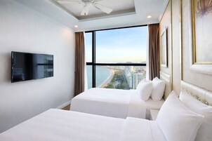 Quarto de hotel com duas camas, televisão, ventoinha no teto e uma grande janela com vista para a cidade.