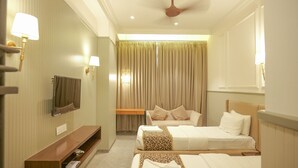 Quarto de hotel com duas camas, televisão, escrivaninha e janela com cortinas.