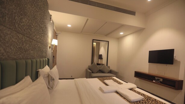 Quarto de hotel com cama, sofá, televisão e espelho.