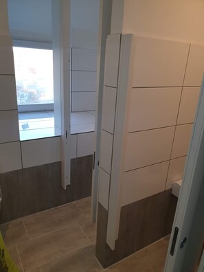Um corredor com paredes em azulejo e janela que dá para área externa.