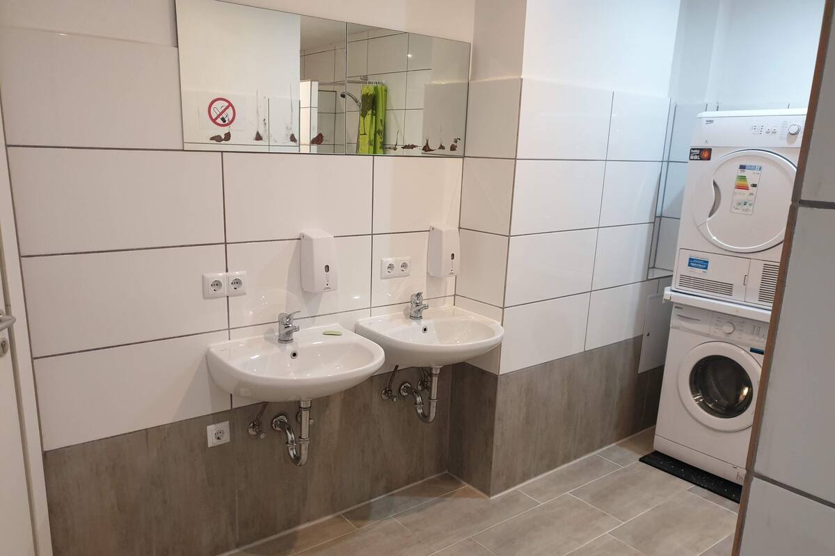 Uma casa de banho moderna com duas pias, um espelho, chuveiro e máquina de lavar roupa.