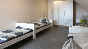 Quarto pequeno e bem iluminado com uma cama de solteiro, um guarda-roupa e uma porta.