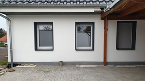 Um edifício com três janelas, telhado de telhas e chão pavimentado.