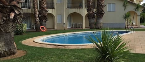 Piscina rodeada por palmeiras e um edifício com várias varandas.