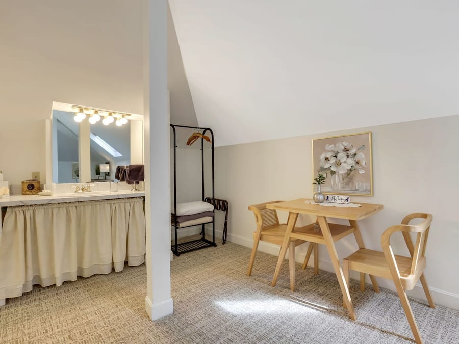 Quarto com um espelho grande, penteadeira e uma pequena mesa de madeira com cadeiras.