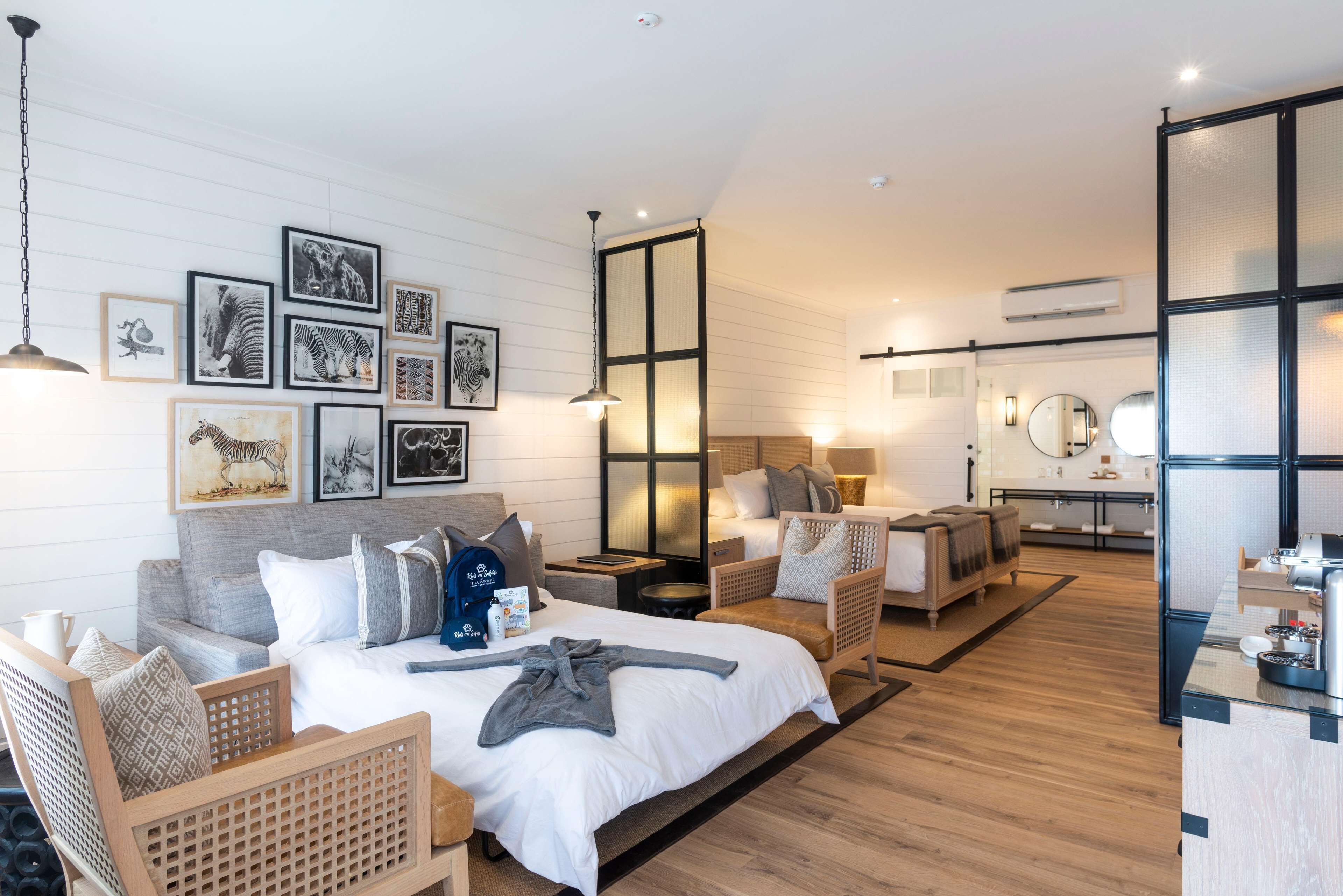 Quarto de hotel moderno com uma cama grande, um sofá, uma cadeira e uma escrivaninha. Há quadros nas paredes e um espelho sobre a escrivaninha.