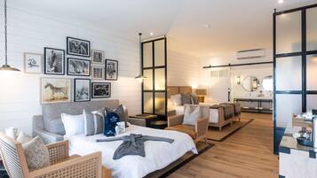 Quarto de hotel moderno com uma cama grande, um sofá, uma cadeira e uma escrivaninha. Há quadros nas paredes e um espelho sobre a escrivaninha.