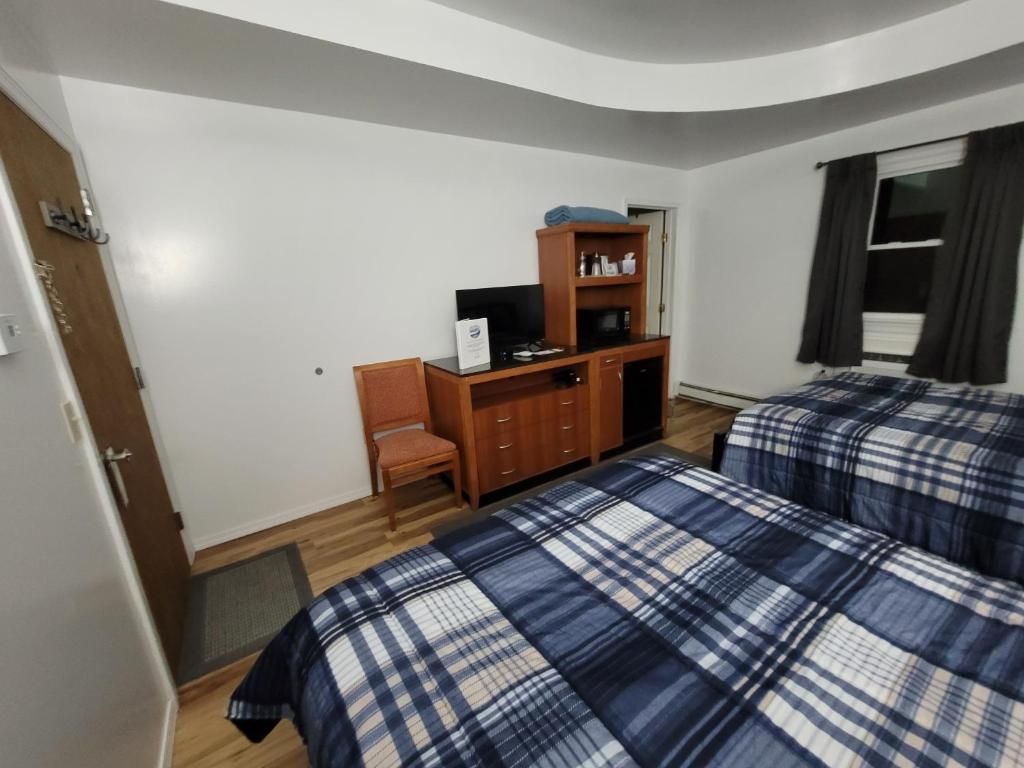 Quarto com duas camas, uma escrivaninha, televisão e guarda-roupa.