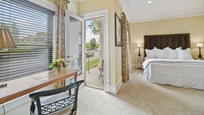 Quarto com uma cama grande, uma mesa com cadeira e vista para o exterior através de uma porta.
