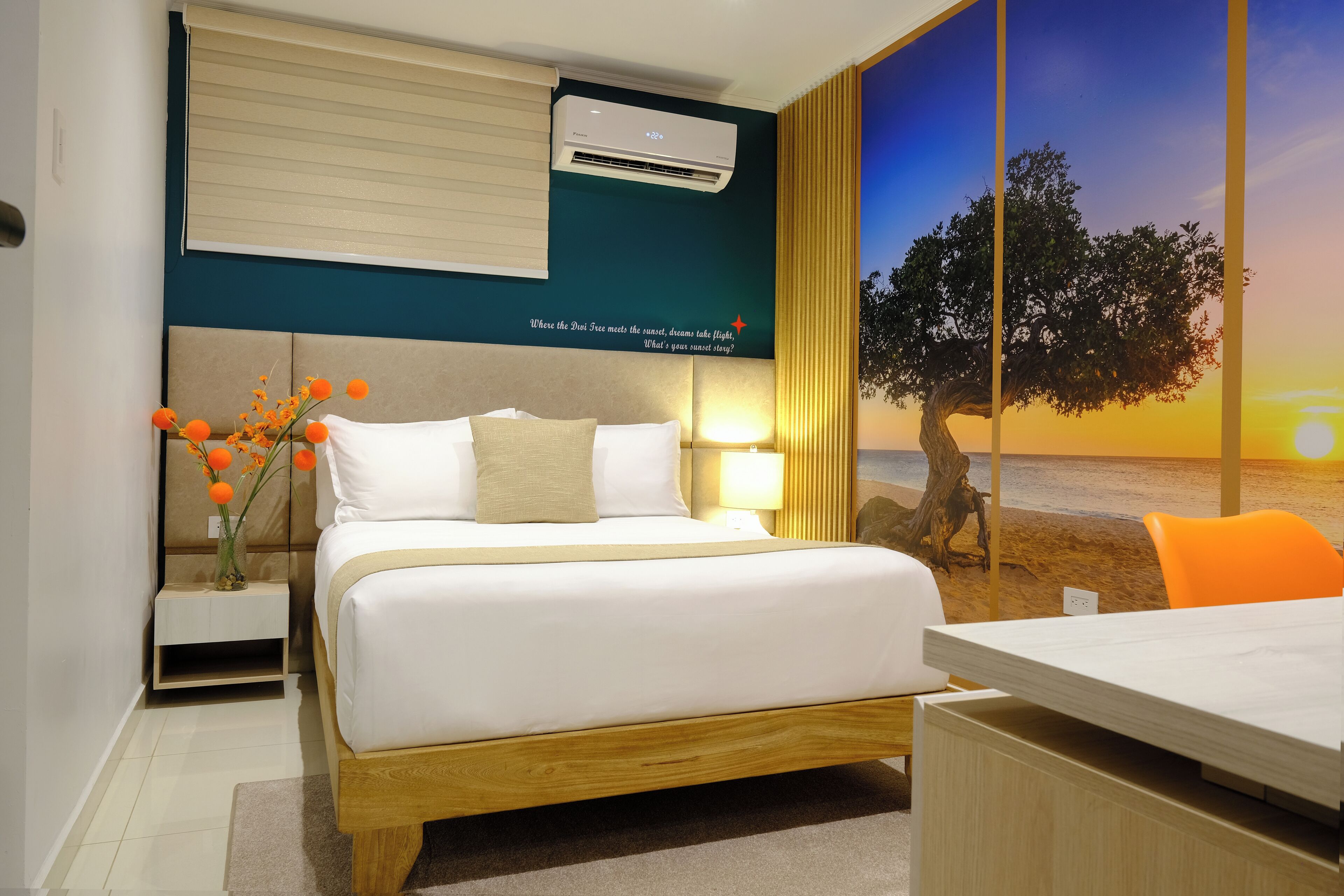 Quarto de hotel moderno com cama, mesa de cabeceira e vista para o pôr do sol através de uma grande janela.