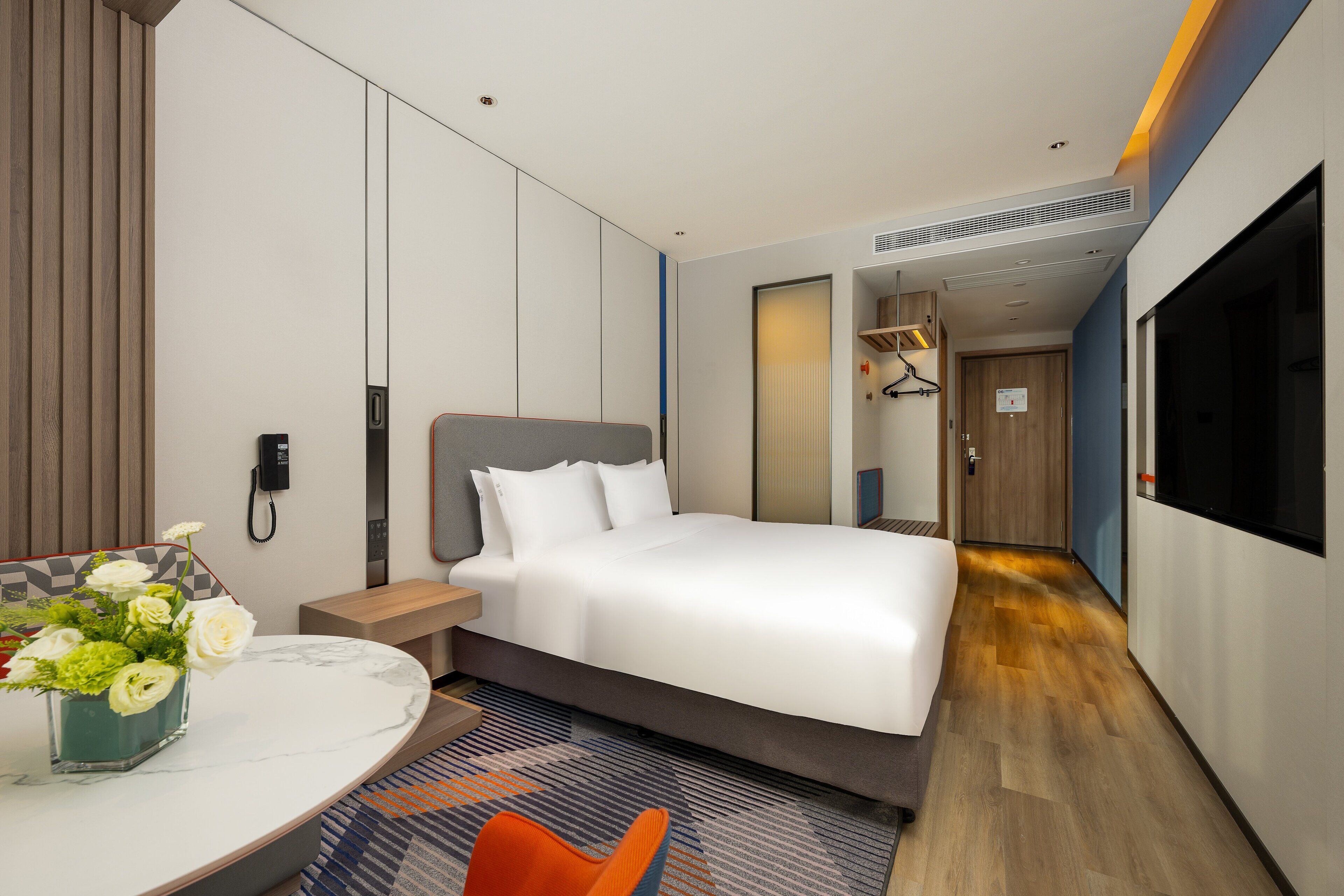 Quarto de hotel moderno com uma cama grande, uma escrivaninha com um vaso de flores, um telefone e uma televisão.