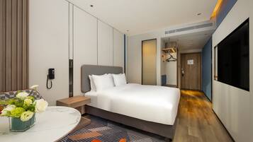 Quarto de hotel moderno com uma cama grande, uma escrivaninha com um vaso de flores, um telefone e uma televisão.