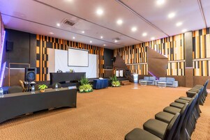 Sala de conferências com palco, tela grande, púlpito e fileiras de cadeiras.