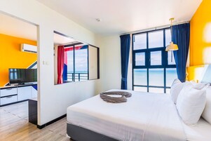Quarto de hotel com cama, televisão, escrivaninha e janela com vista para o mar.