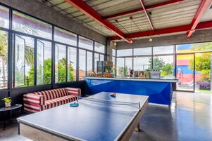 Um quarto espaçoso com mesa de pingue-pongue, área de bar com diversos frascos e grandes janelas com vista para o exterior.
