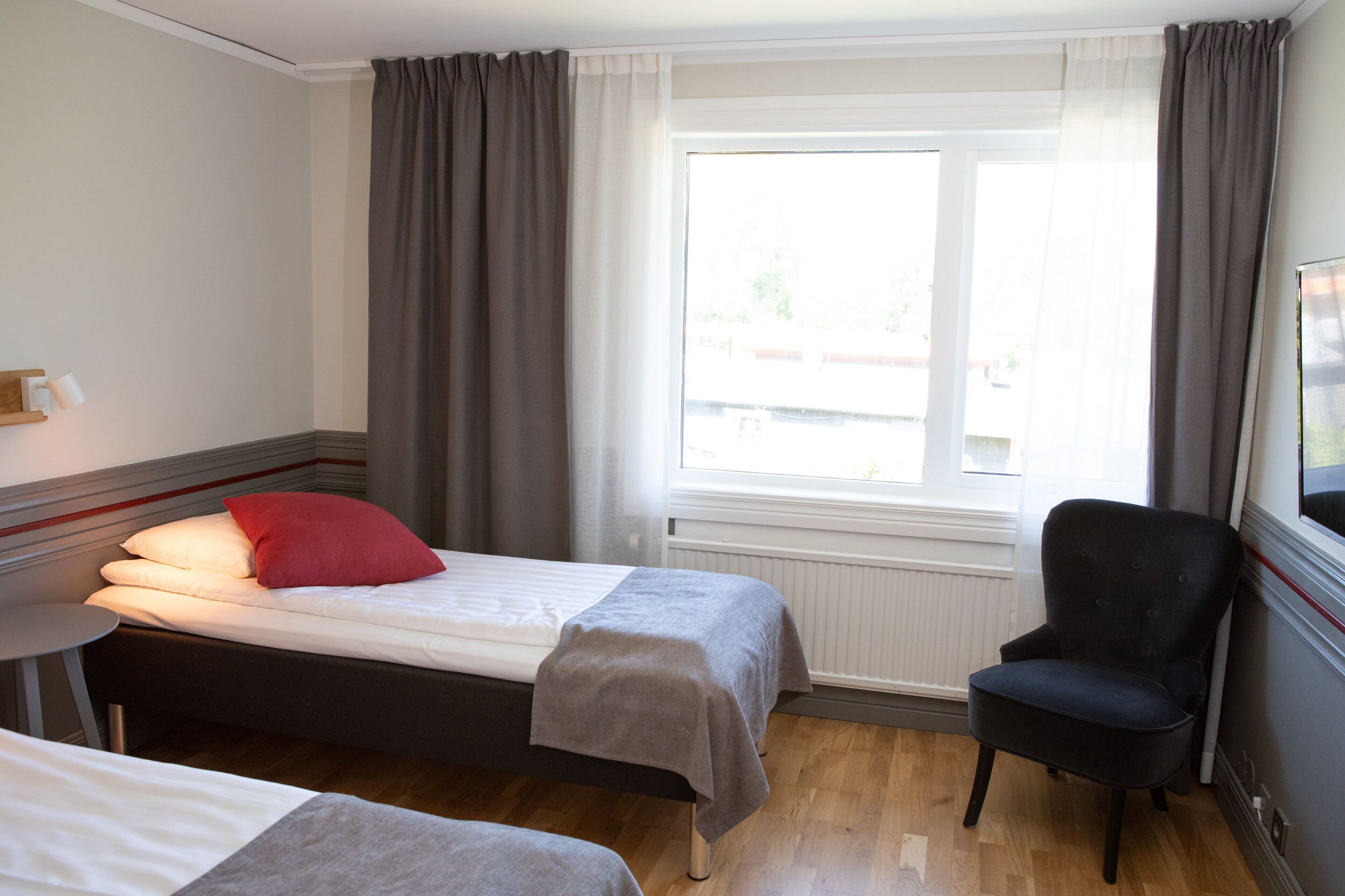 Quarto de hotel com duas camas, uma cadeira, uma janela com cortinas e um radiador.