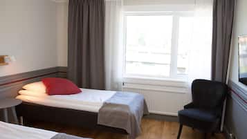 Quarto de hotel com duas camas, uma cadeira, uma janela com cortinas e um radiador.
