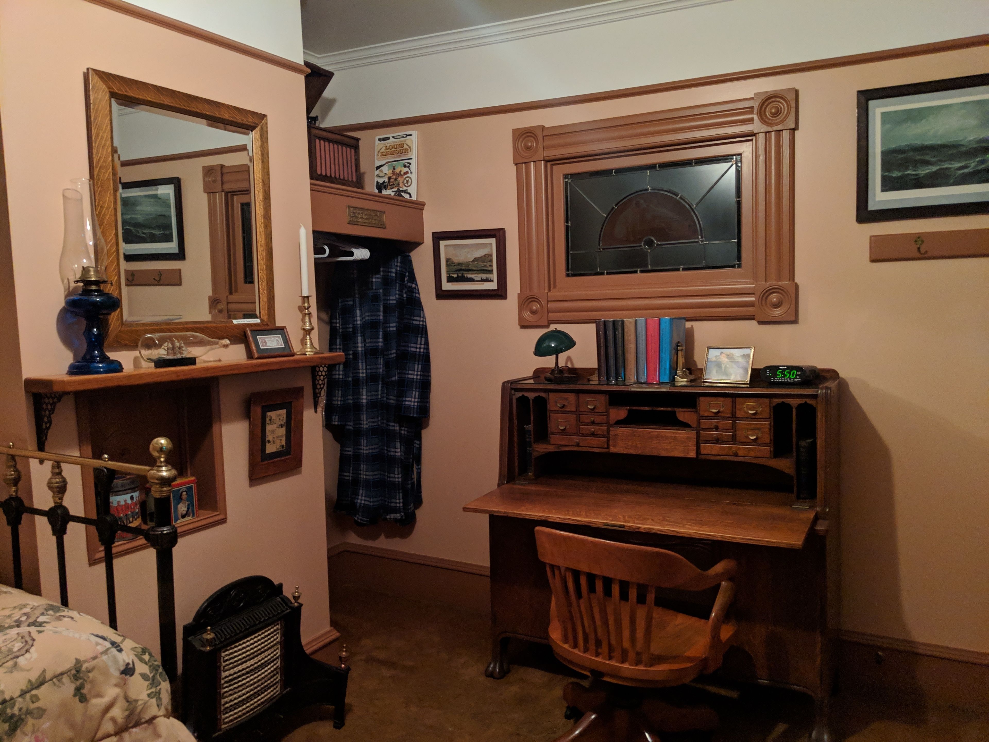 Quarto com escrivaninha de madeira, uma cadeira, um espelho, um relógio e um quadro na parede.