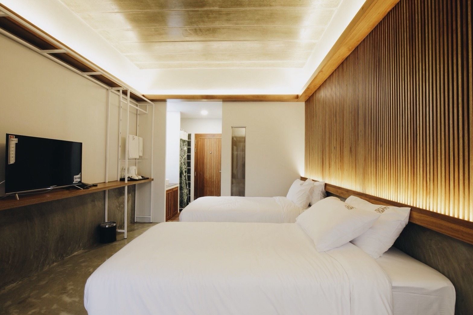 Quarto de hotel com uma cama grande, uma televisão, uma escrivaninha com computador e um painel de parede em madeira.