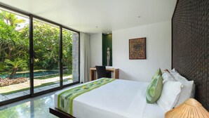Quarto moderno com uma cama grande, uma escrivaninha e vista para uma piscina e vegetação.