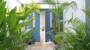 Um caminho leva a uma porta, com um chuveiro fixado na parede e painéis decorativos.