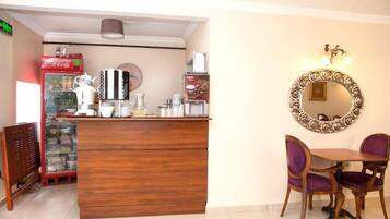 Uma área de recepção com balcão de madeira, refrigerador de Coca-Cola, máquina de café e espelho na parede.