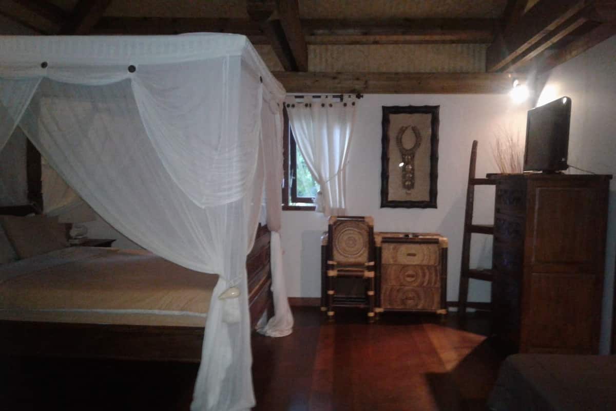 Quarto com cama de dossel, cômoda de madeira e mesa de cabeceira.