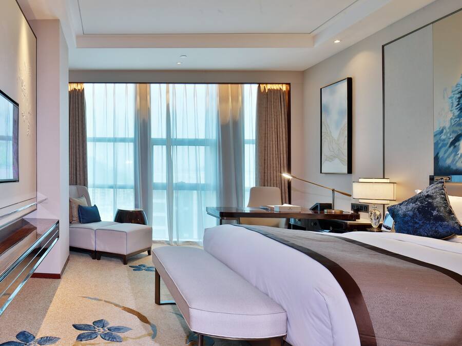Quarto de hotel com uma cama grande, um sofá, uma escrivaninha e uma televisão.