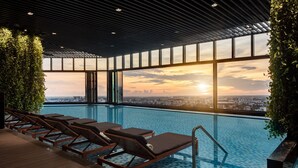 Piscina infinita no terraço com espreguiçadeiras e vista para a cidade ao pôr do sol.