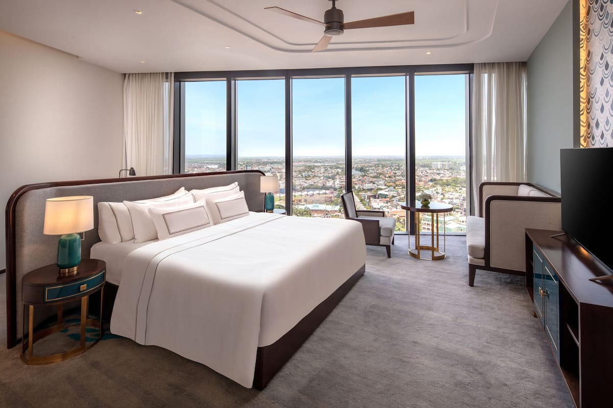 Quarto de hotel moderno com uma cama grande, televisão, escrivaninha e vista para a cidade.